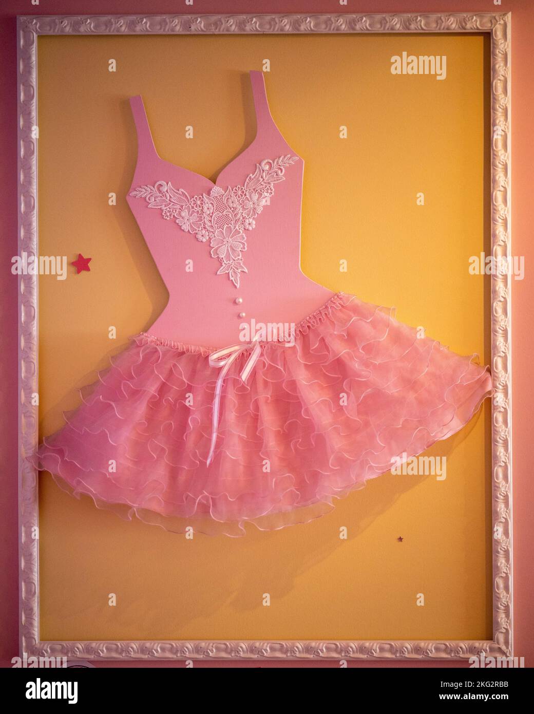 A pink ballerina dress hanging on a mirror frame isolated on a pink ...