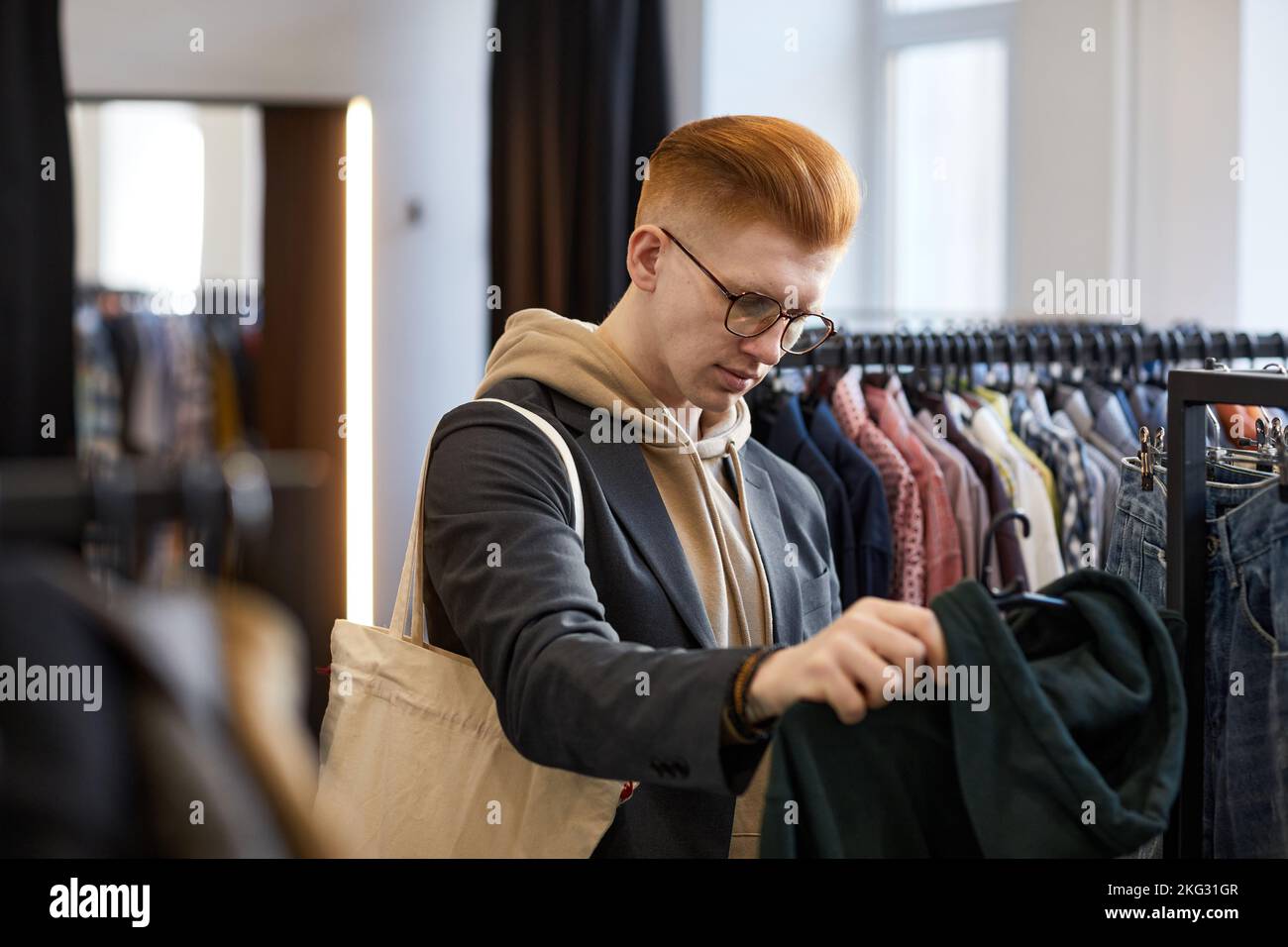 Young red haired man browsing clothes on racks while shopping ...