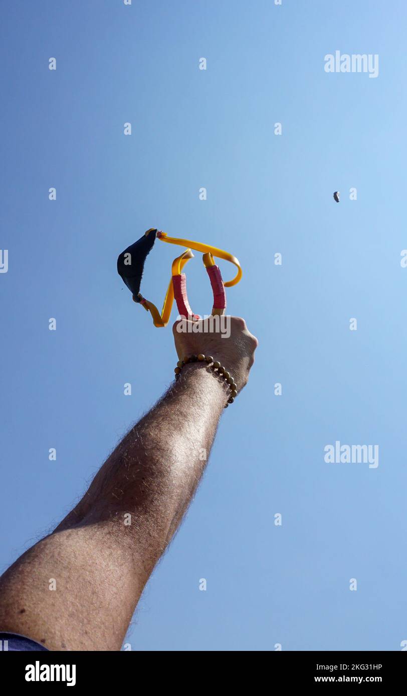 A man using a handmade rubber slingshot against a blurred background ...