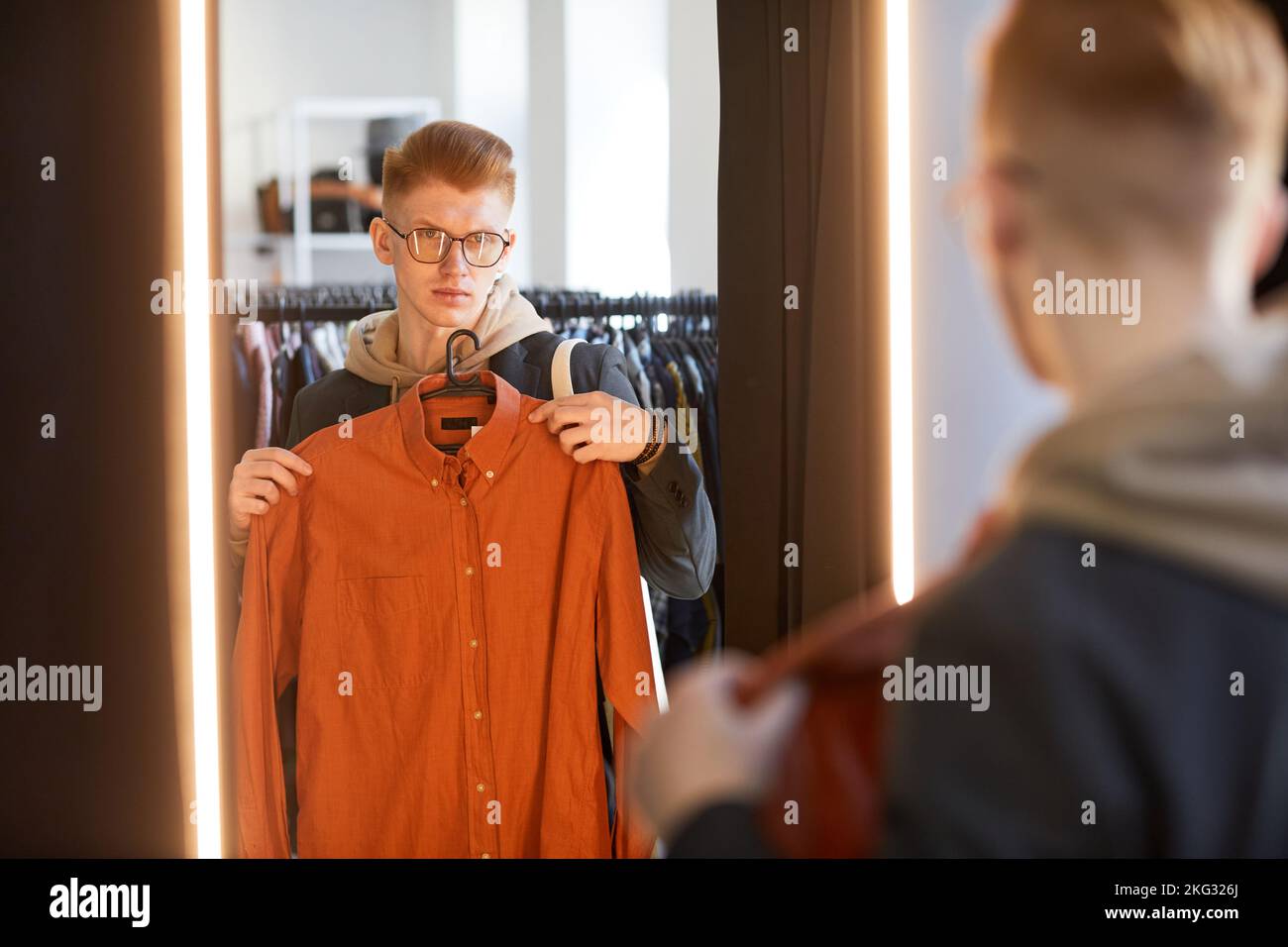 Moody portrait of young man trying on clothes in fitting room at thrift ...