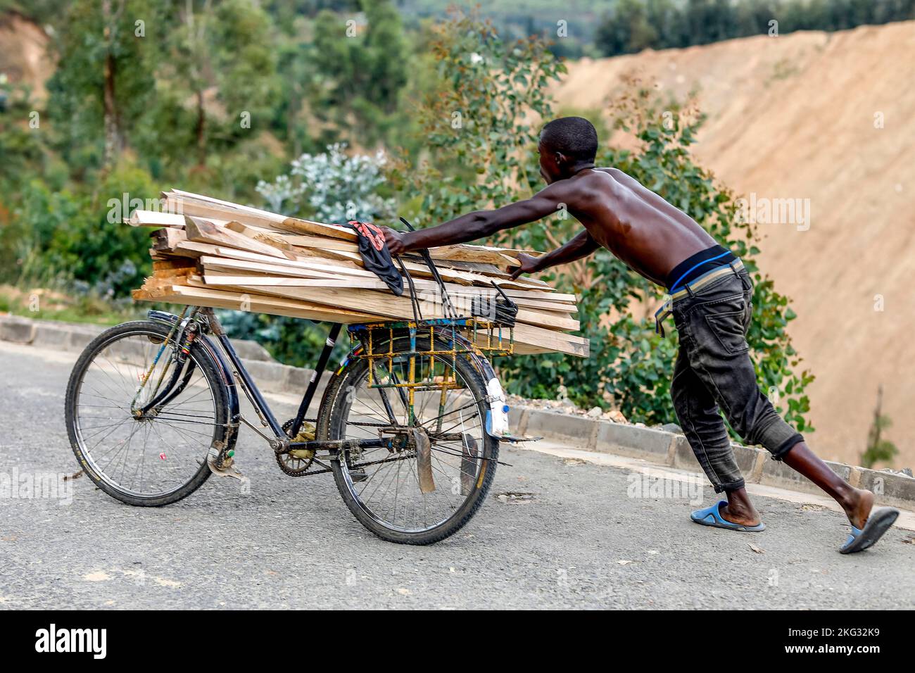Young man pushing a bike loaded with planks in western Rwanda Stock ...
