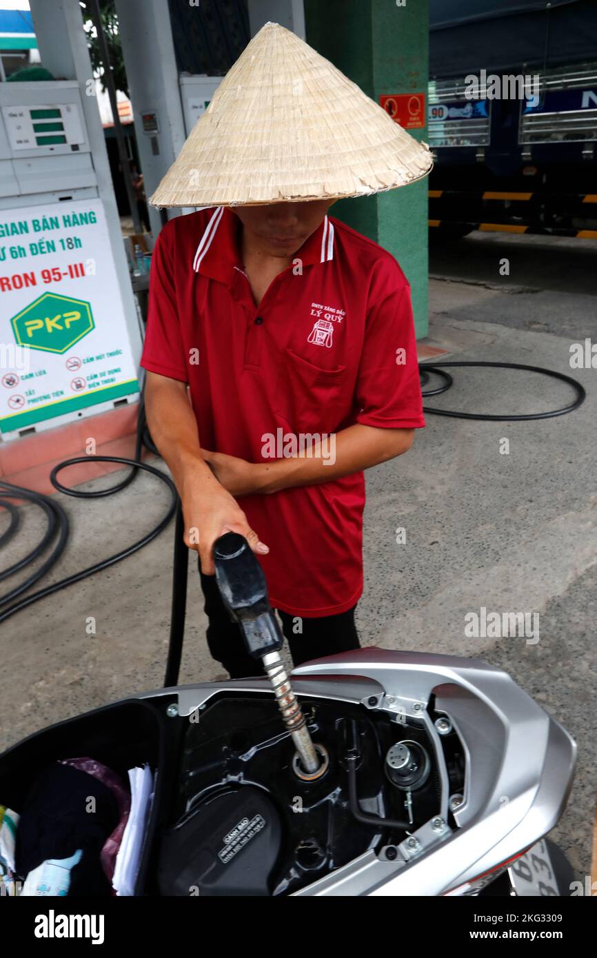 Petrol gas station. Man with conical hat filling up a customers scooter ...