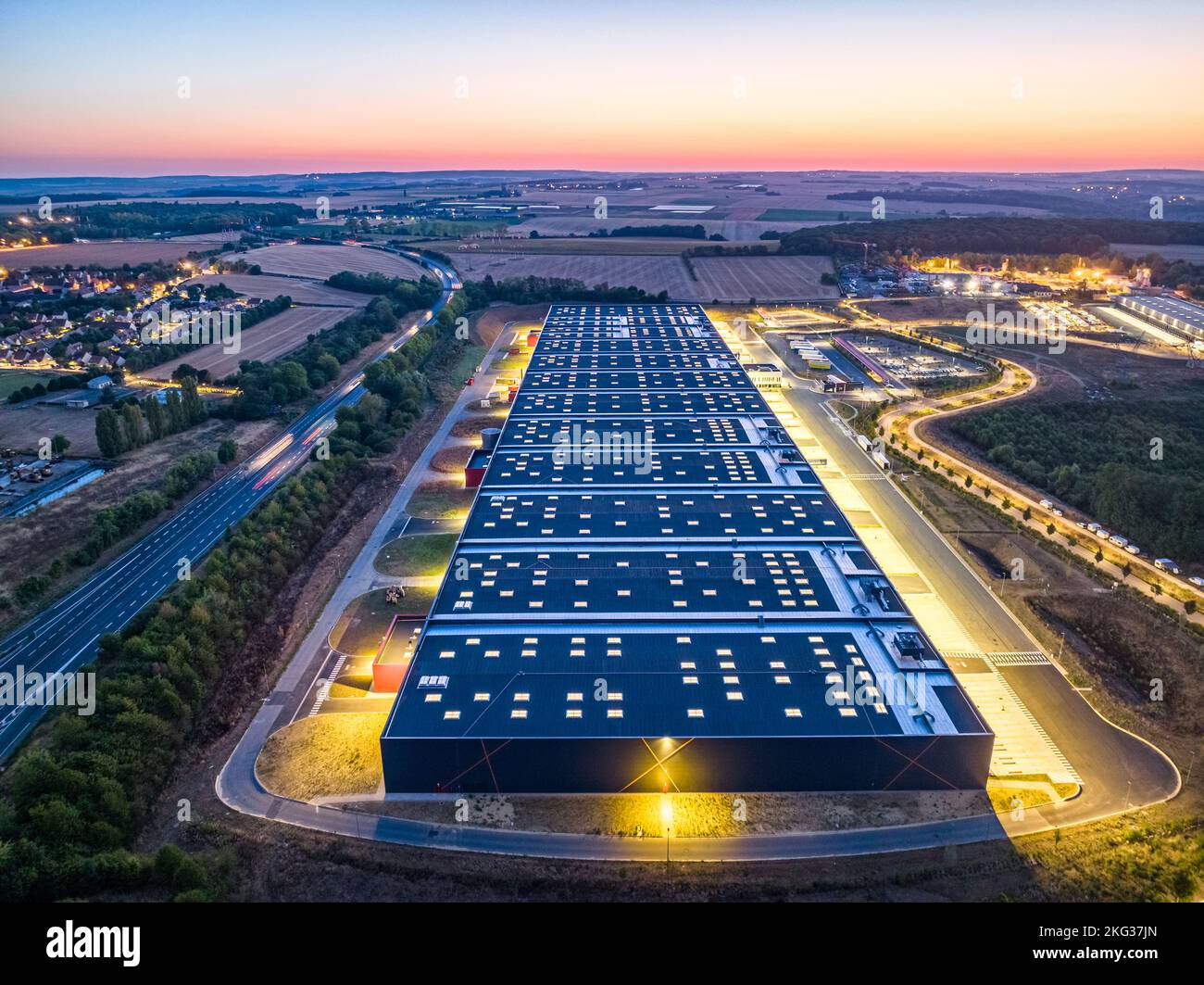 Drone evening shot of warehouse industry surrounded with greenery and ...