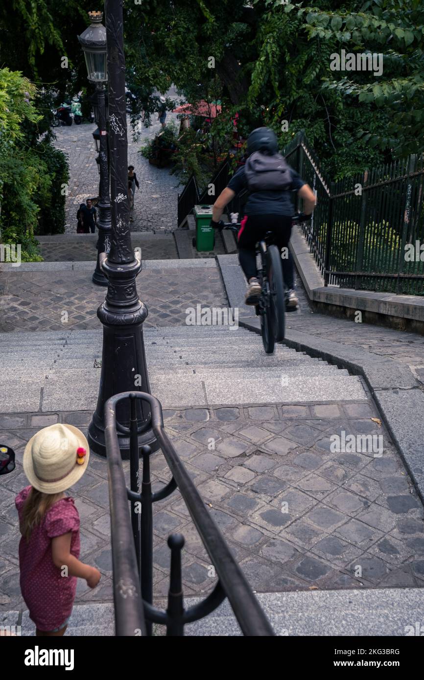 A biker going down stairs with his bike while a young girl looking at him in Montmartre, Paris ...