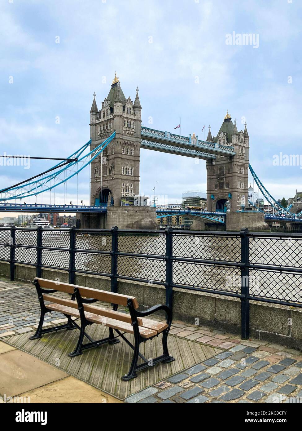 A vertical low-angle of Tower Bridge from a platform with a bench ...
