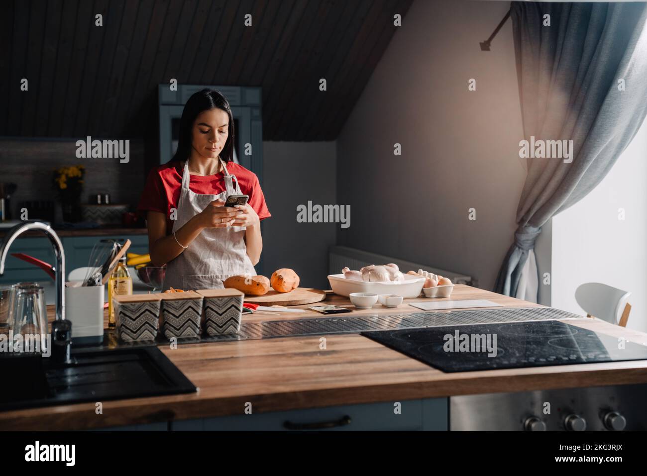 Young hispanic woman wearing apron using cellphone while cooking in ...