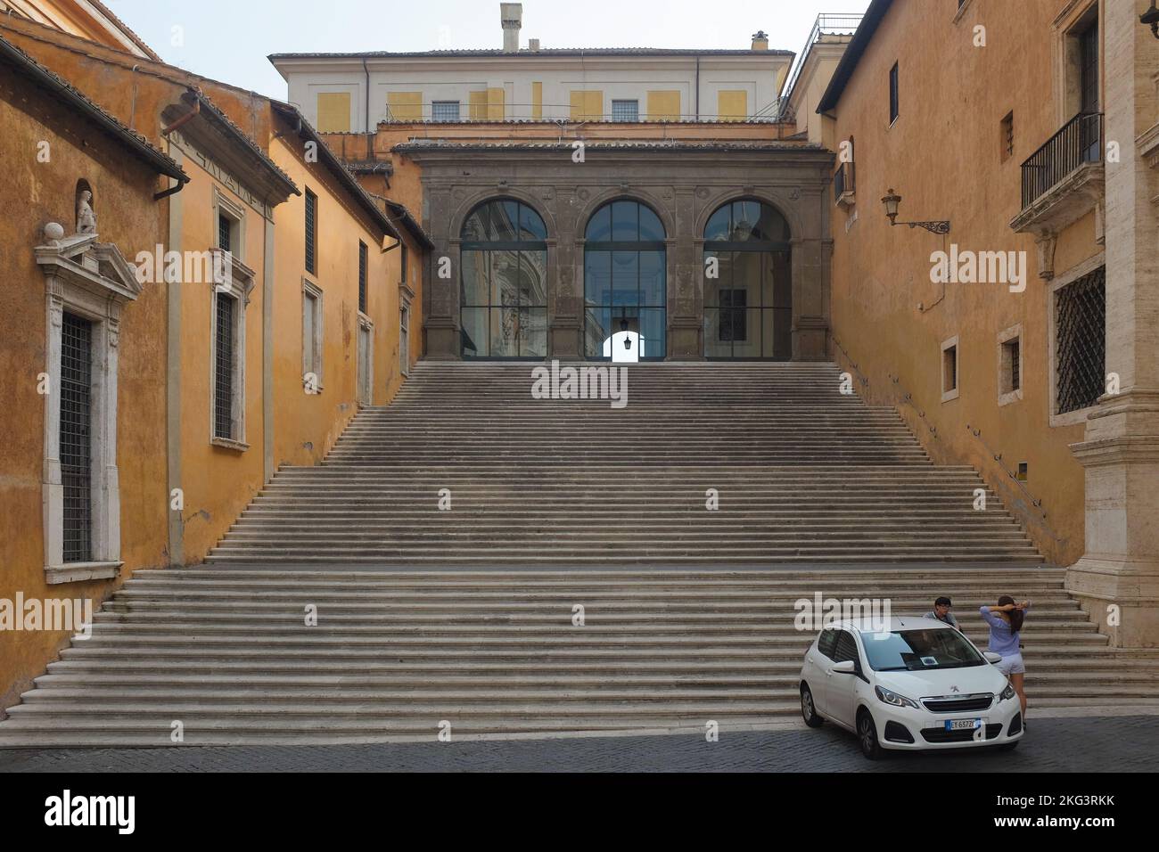Man and woman relax outside a small white car parked at the foot of the ...
