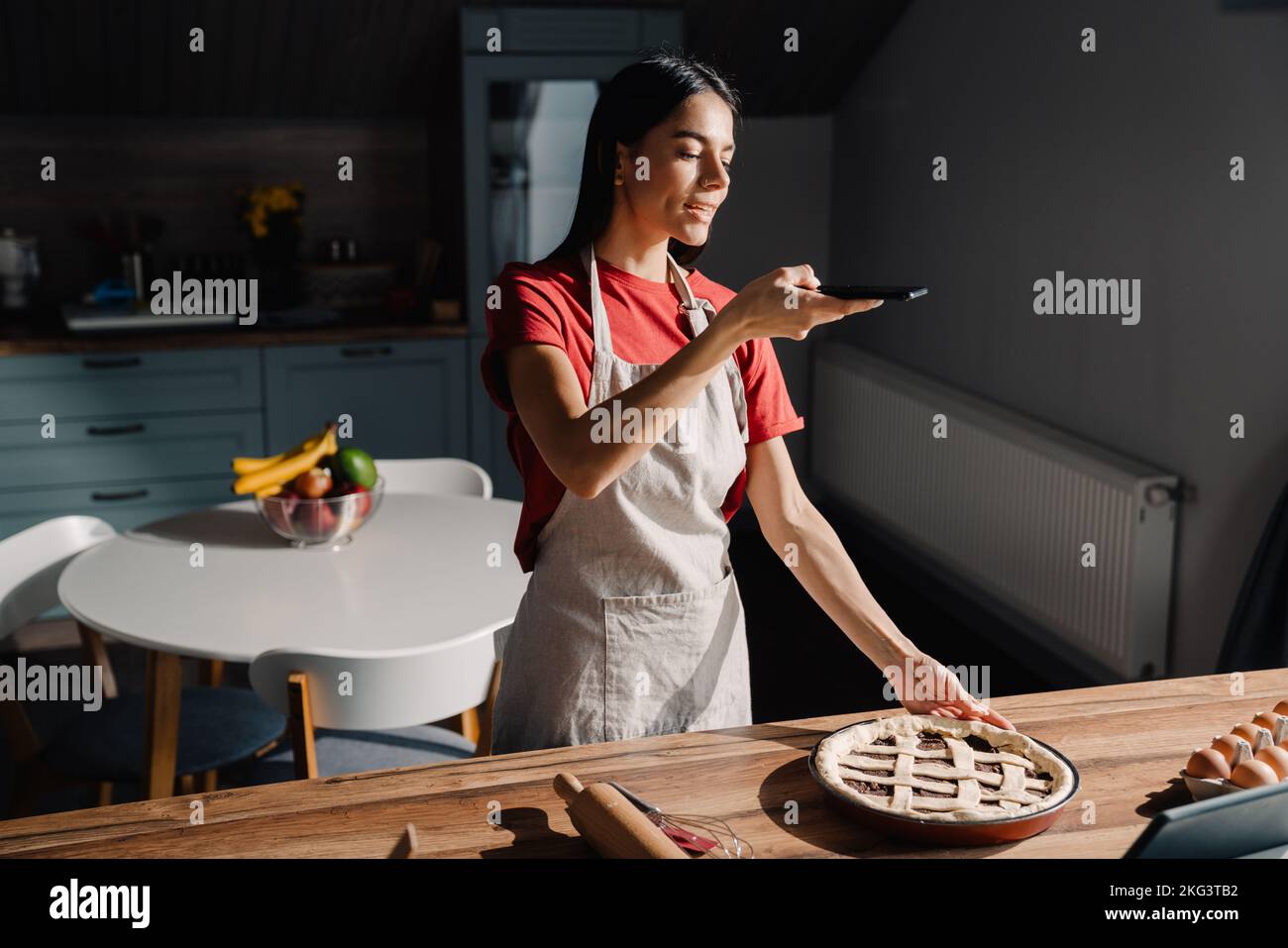 Young hispanic brunette woman wearing apron taking photo of meal while ...