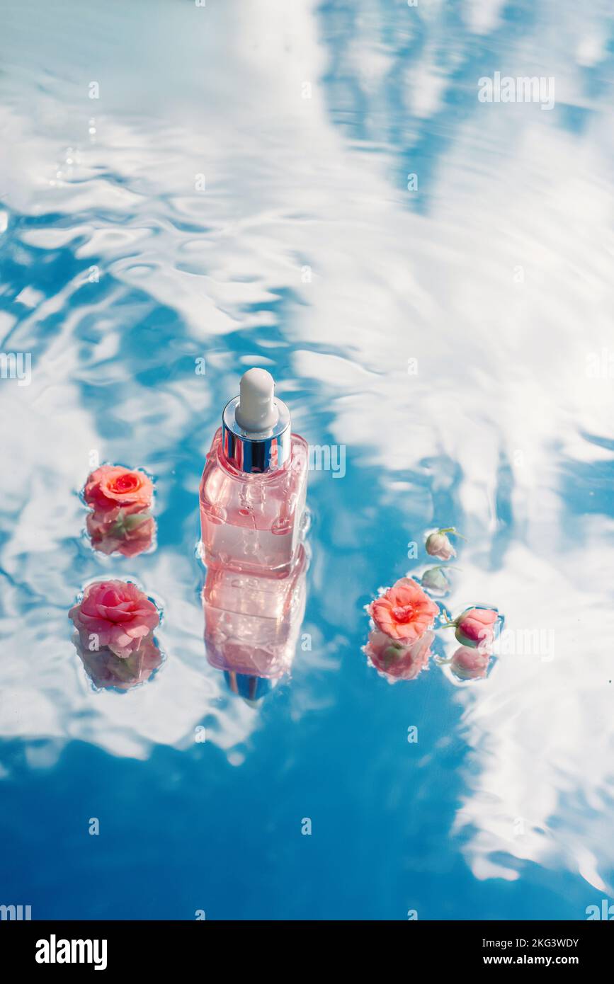 Pink transparent bottle with rose oil, serum on a water background with ...