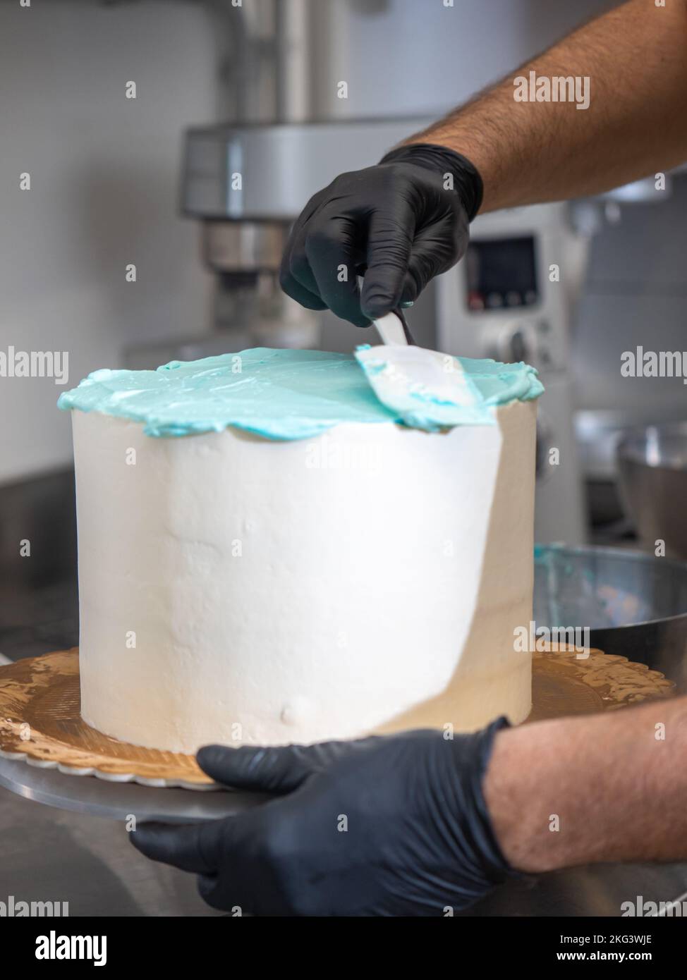 cake designer smoothing a frosted blank cake with turquoise light blue ...