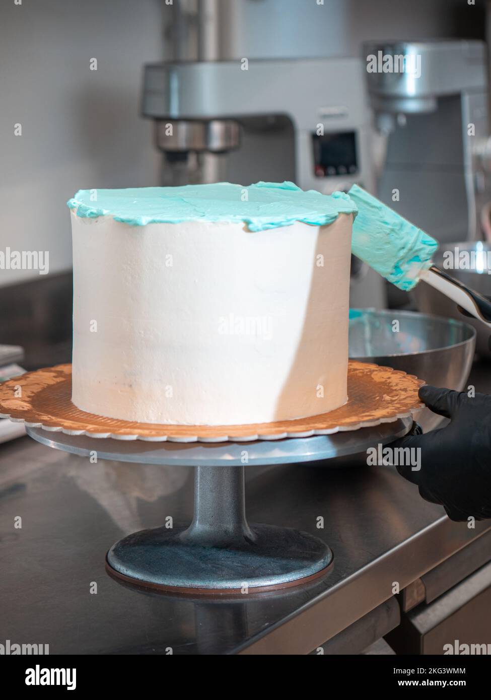 cake designer smoothing a frosted blank cake with turquoise light blue ...