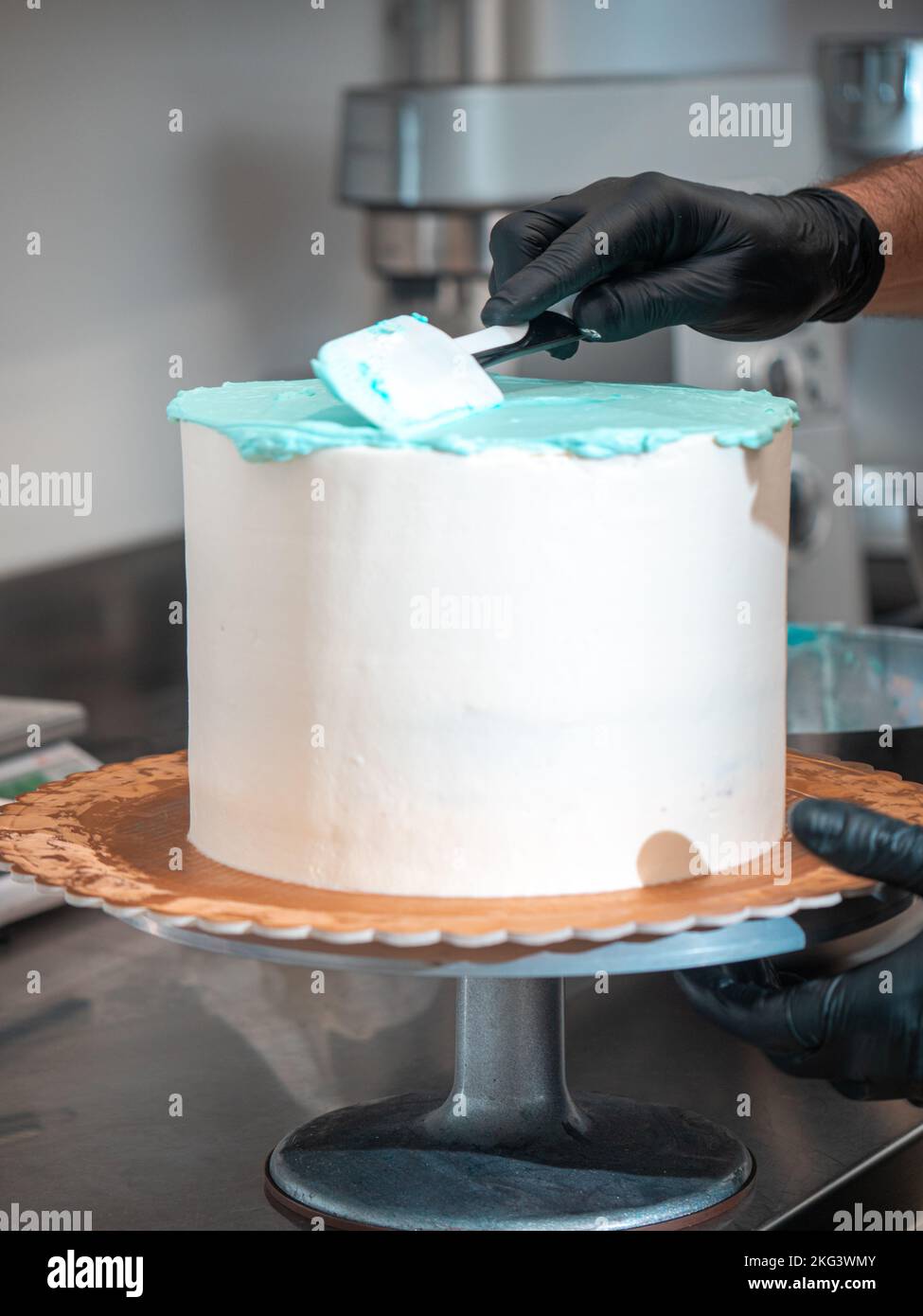 cake designer smoothing a frosted blank cake with turquoise light blue ...