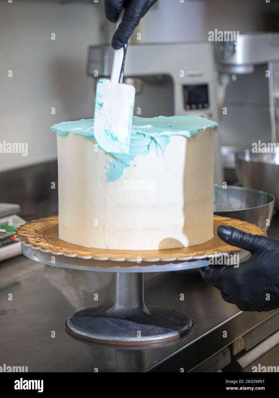 cake designer smoothing a frosted blank cake with turquoise light blue ...