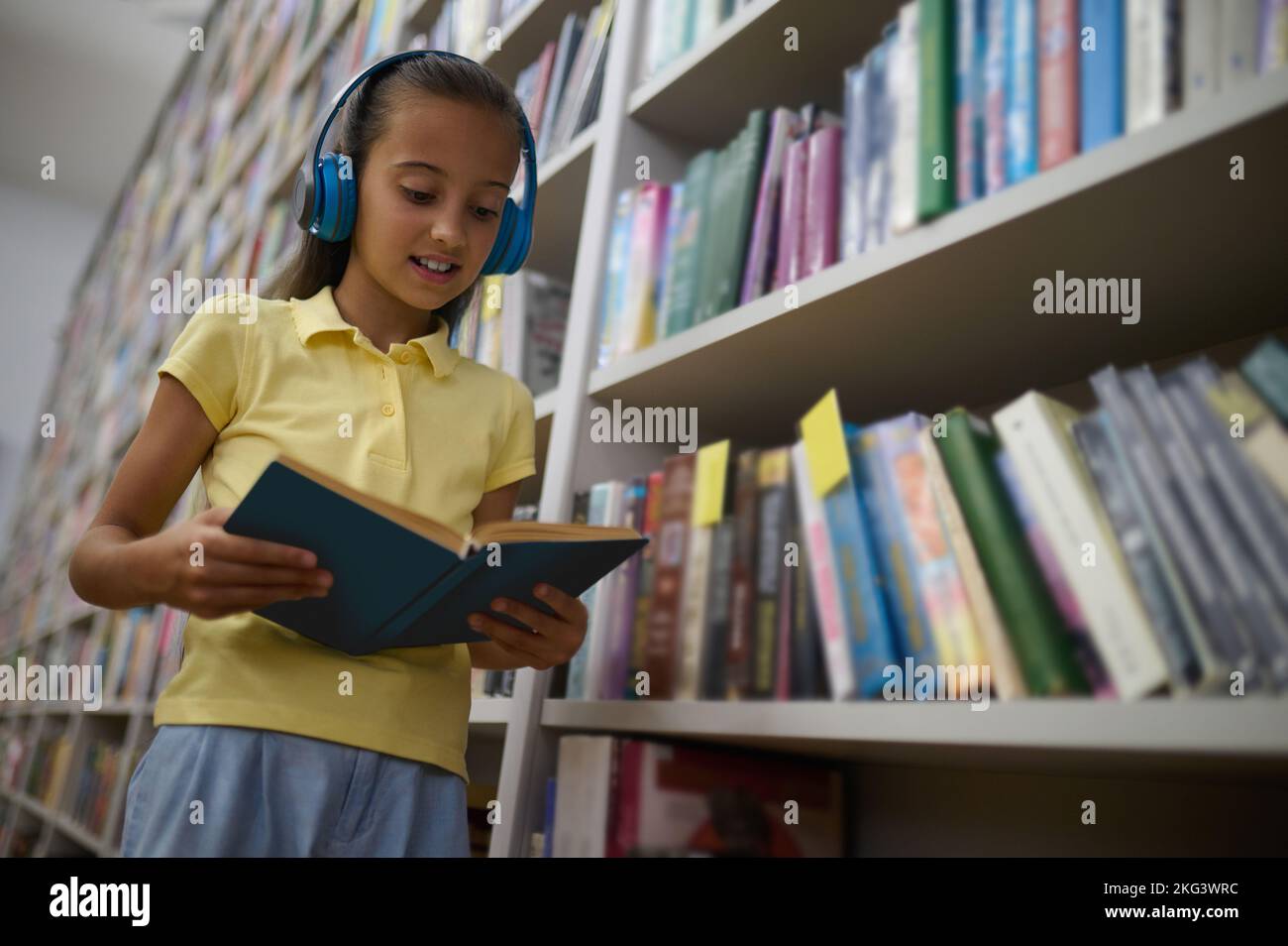 Girl in headphones reading a book in the library Stock Photo - Alamy