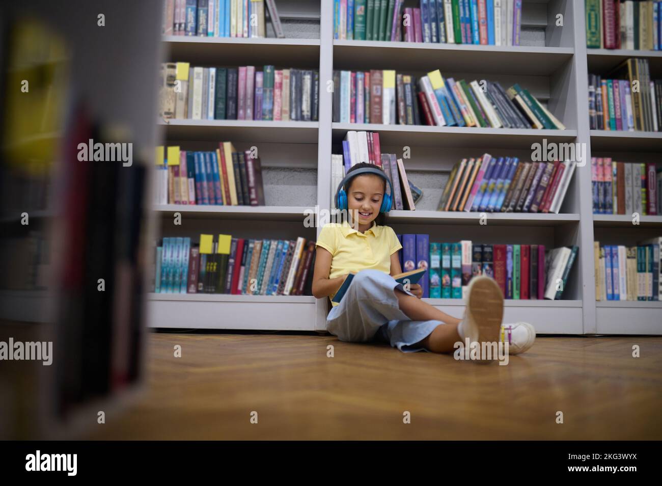 Girl in yellow tshirt sitting on floor in the library and listening to ...