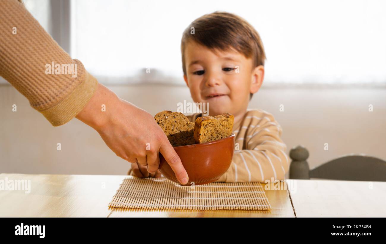 a young mother serves her son a healthy breakfast and sits next to the ...