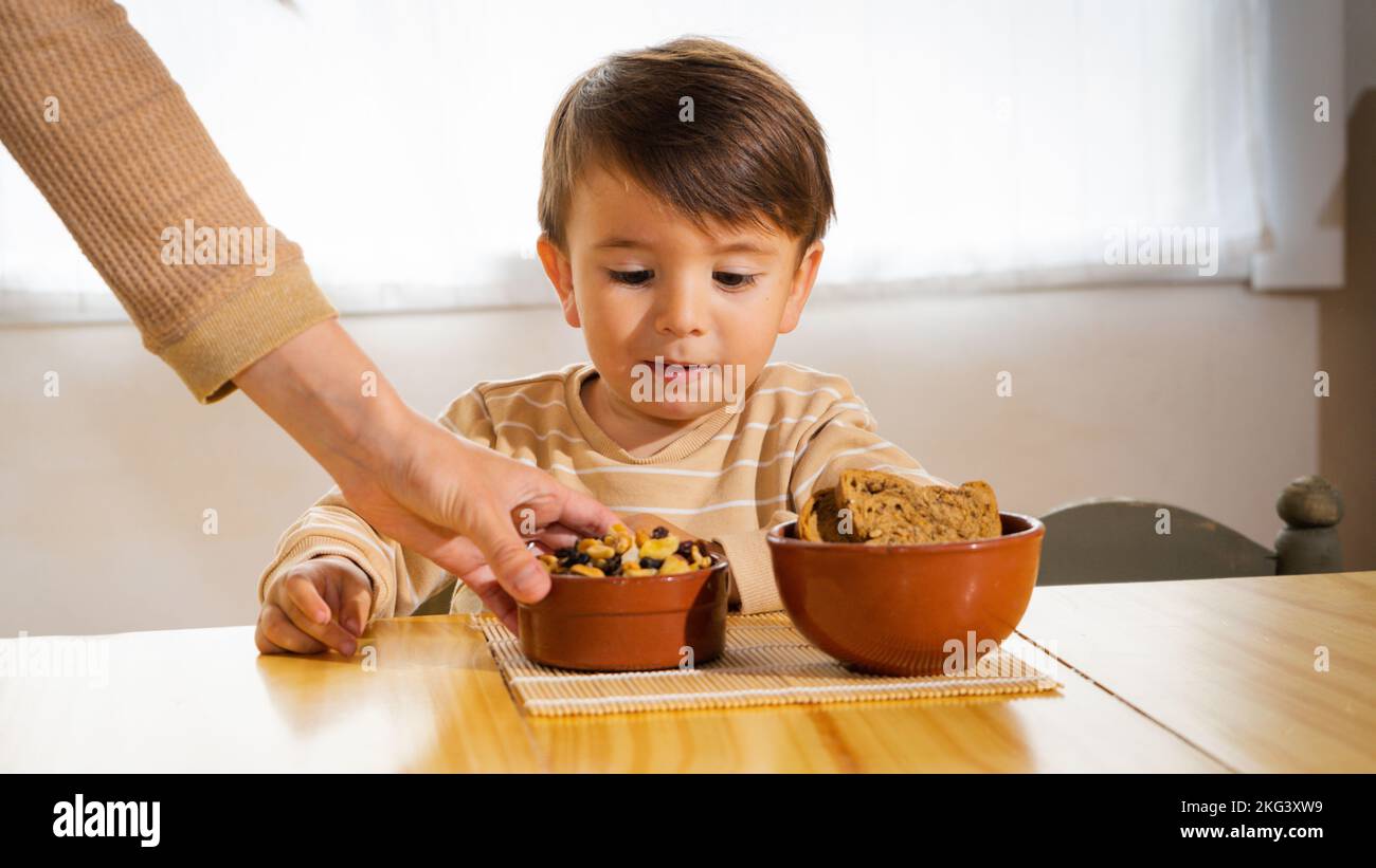 a young mother serves her son a healthy breakfast and sits next to the ...