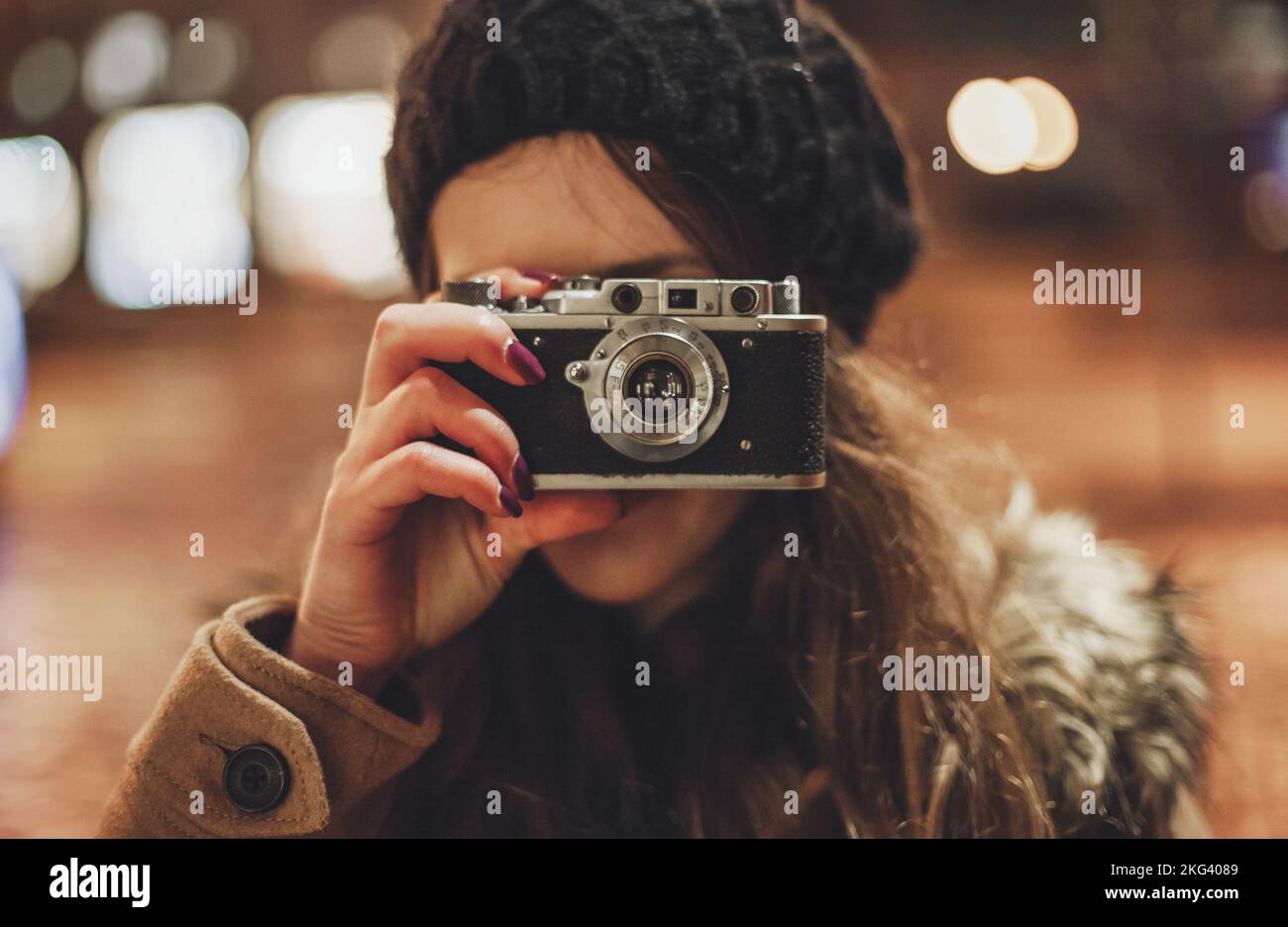 Hipster girl with retro camera taking photos in the night city street ...