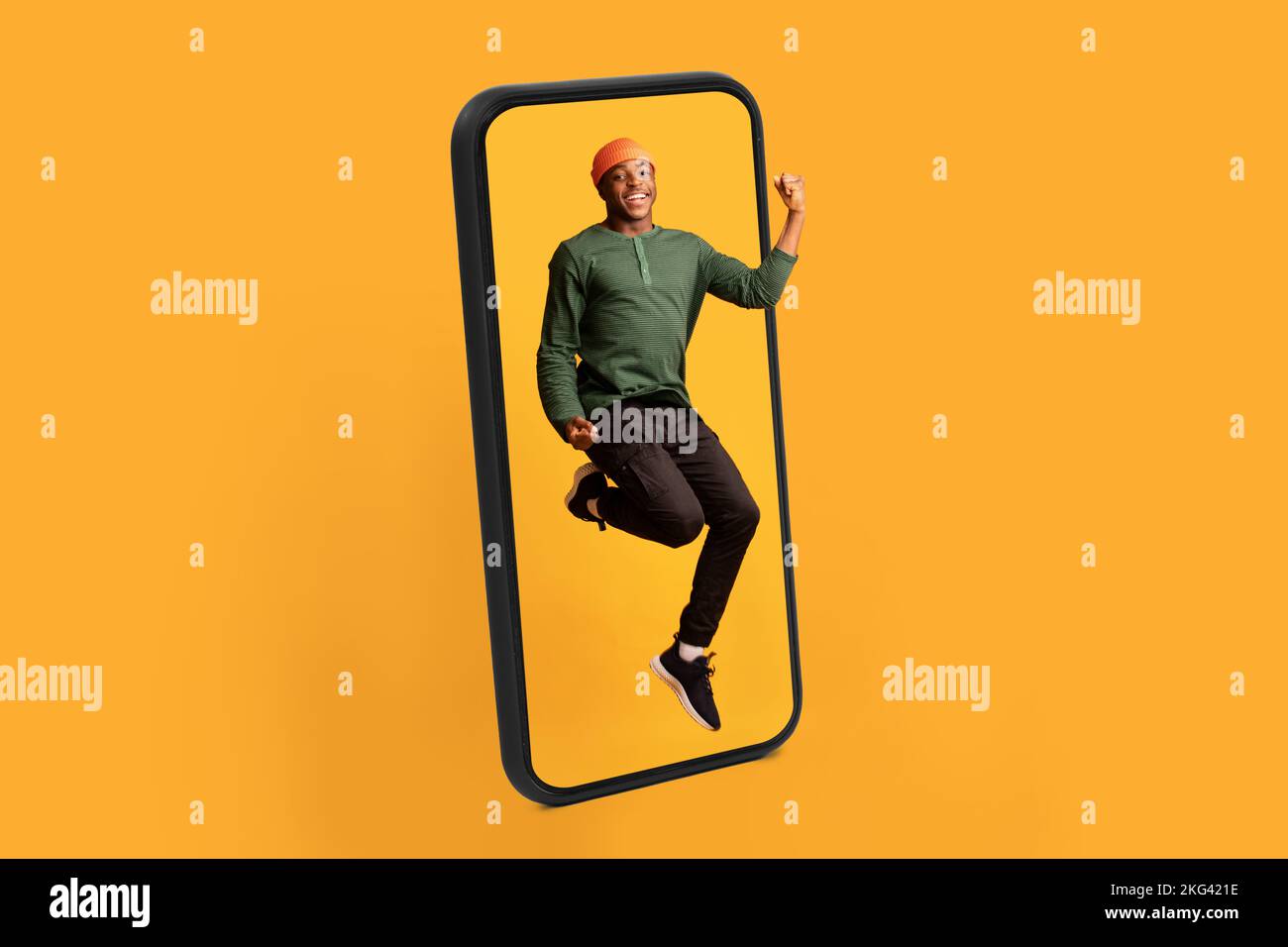 Cheerful excited millennial black guy jumping from huge smartphone ...
