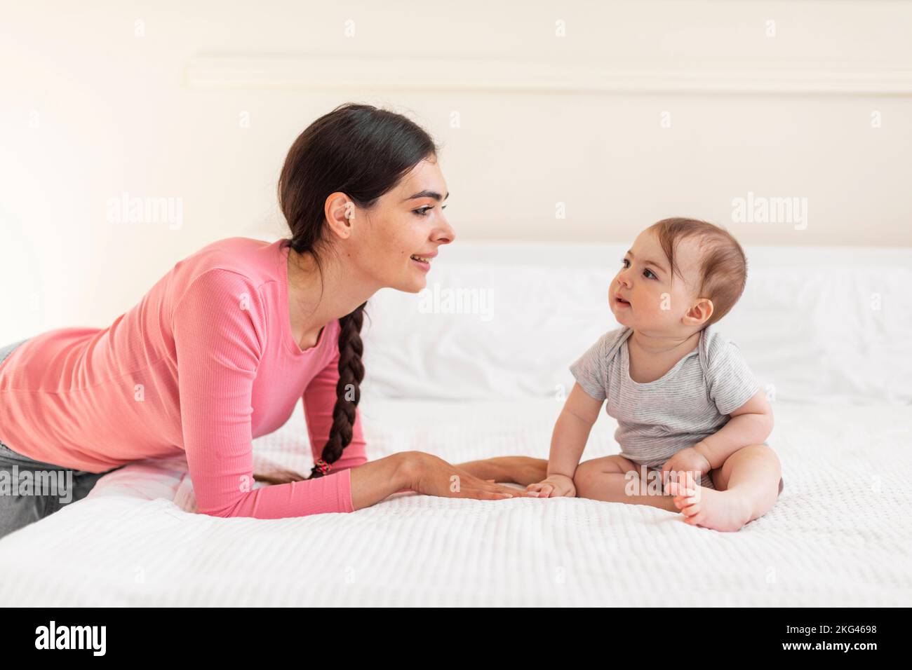 Happy young mom resting with baby girl on bed, adorable child sitting ...
