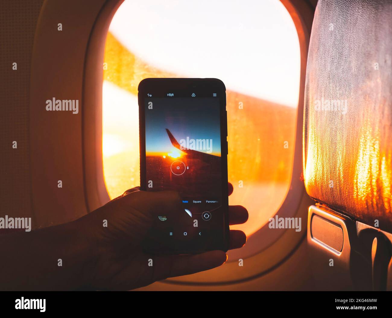 Taking photo of sunset from an airplane window. Hand holding phone ...