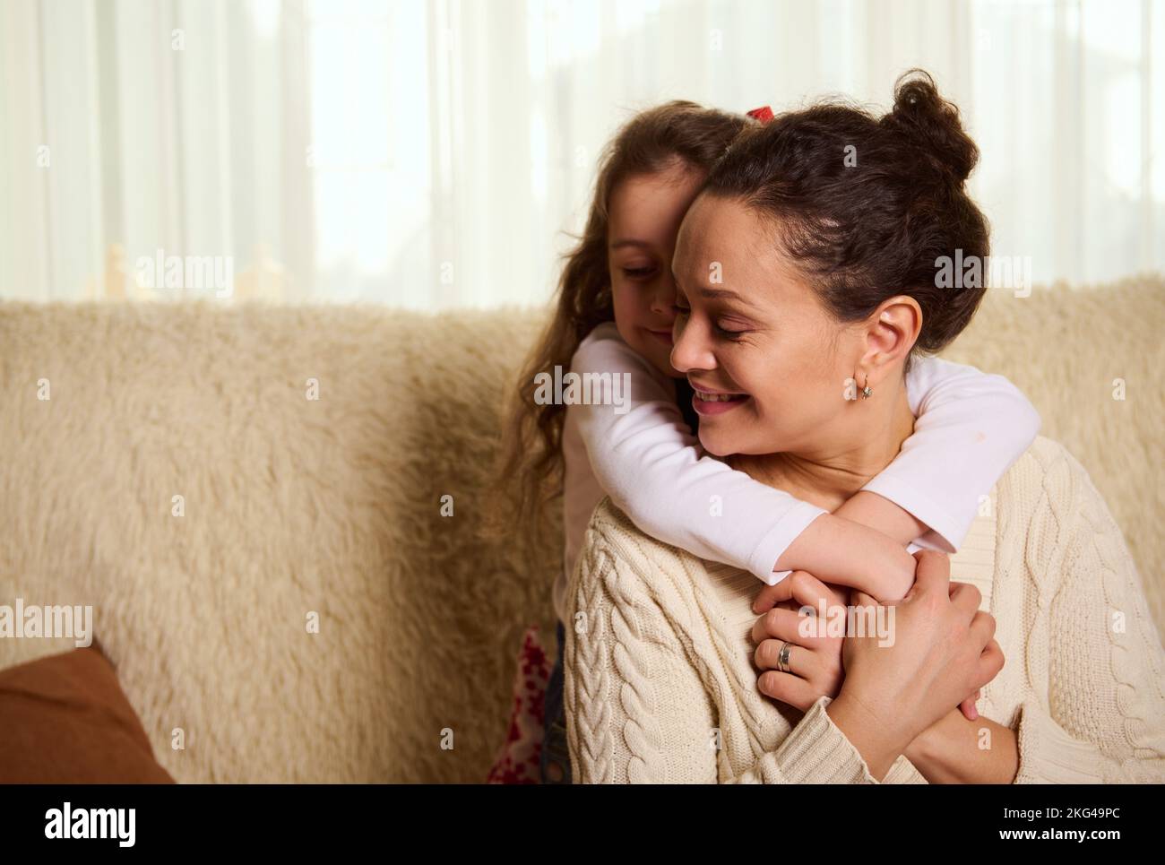 Beautiful little child, daughter hugging her mum from the back, sitting ...