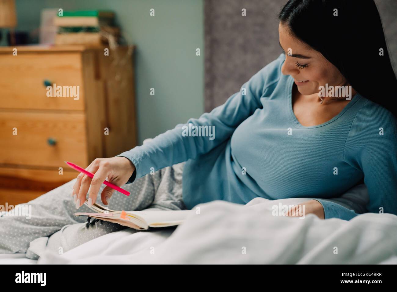 Young hispanic woman writing down notes at organizer while lying in bed ...