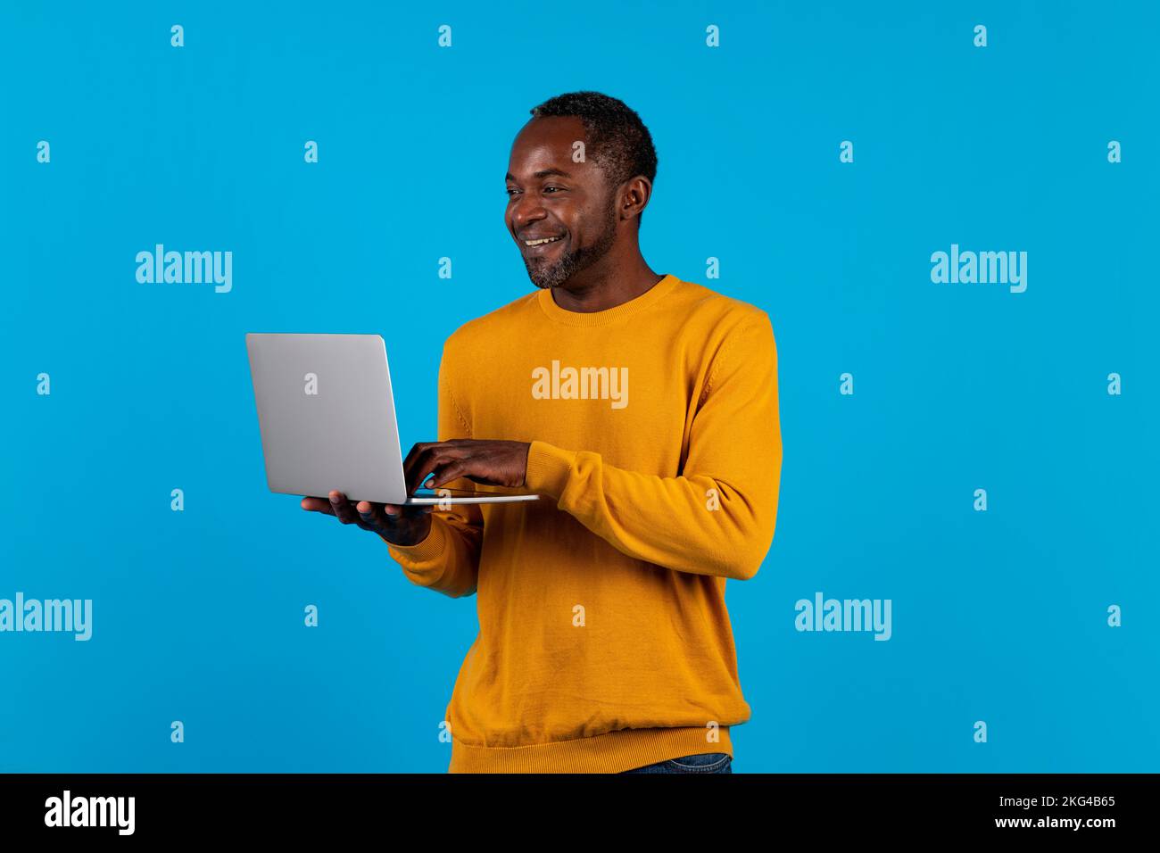 Happy african american adult man using computer on blue Stock Photo - Alamy