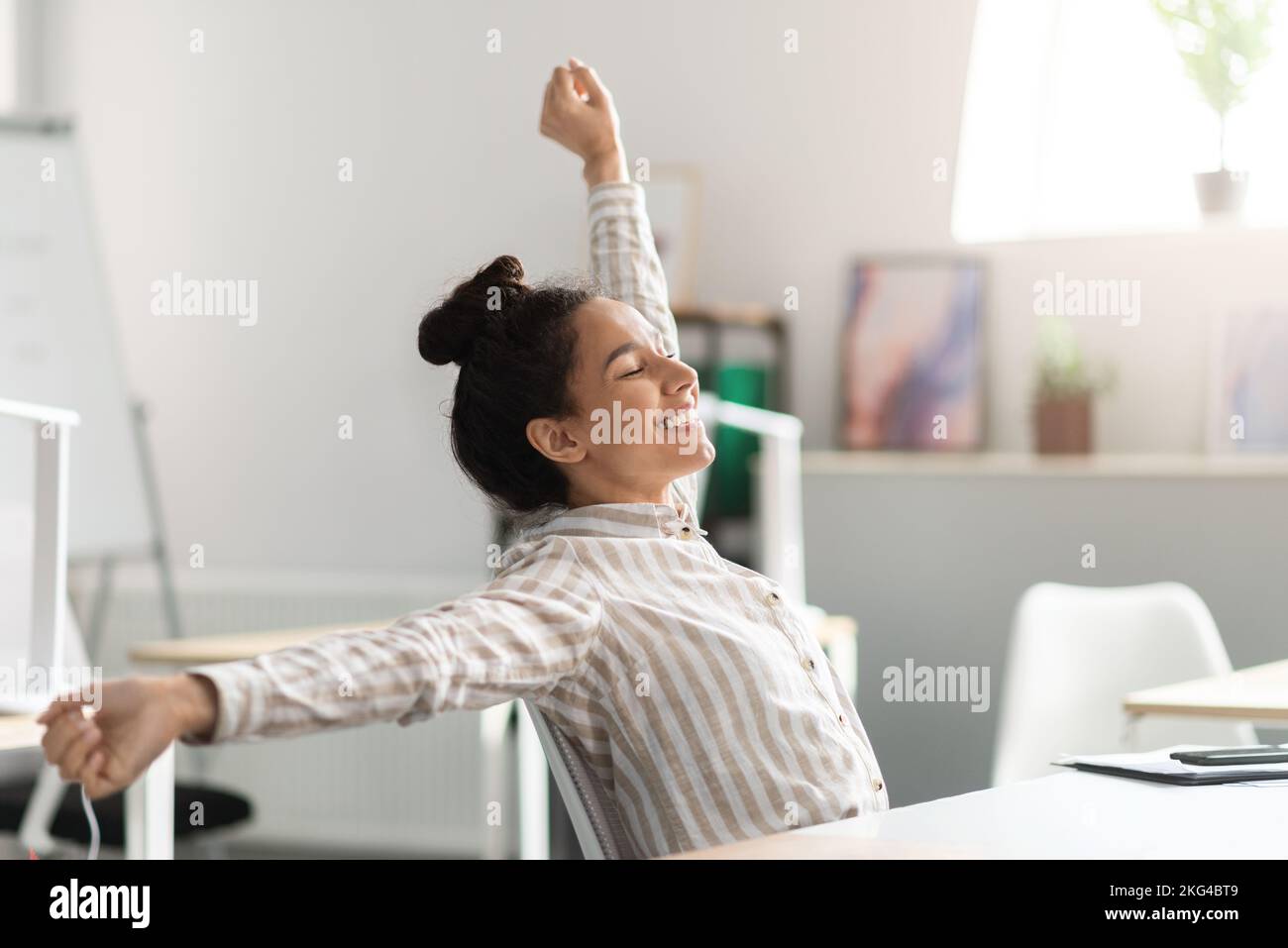 Relax at work. Happy young female manager sitting in office, stretching ...