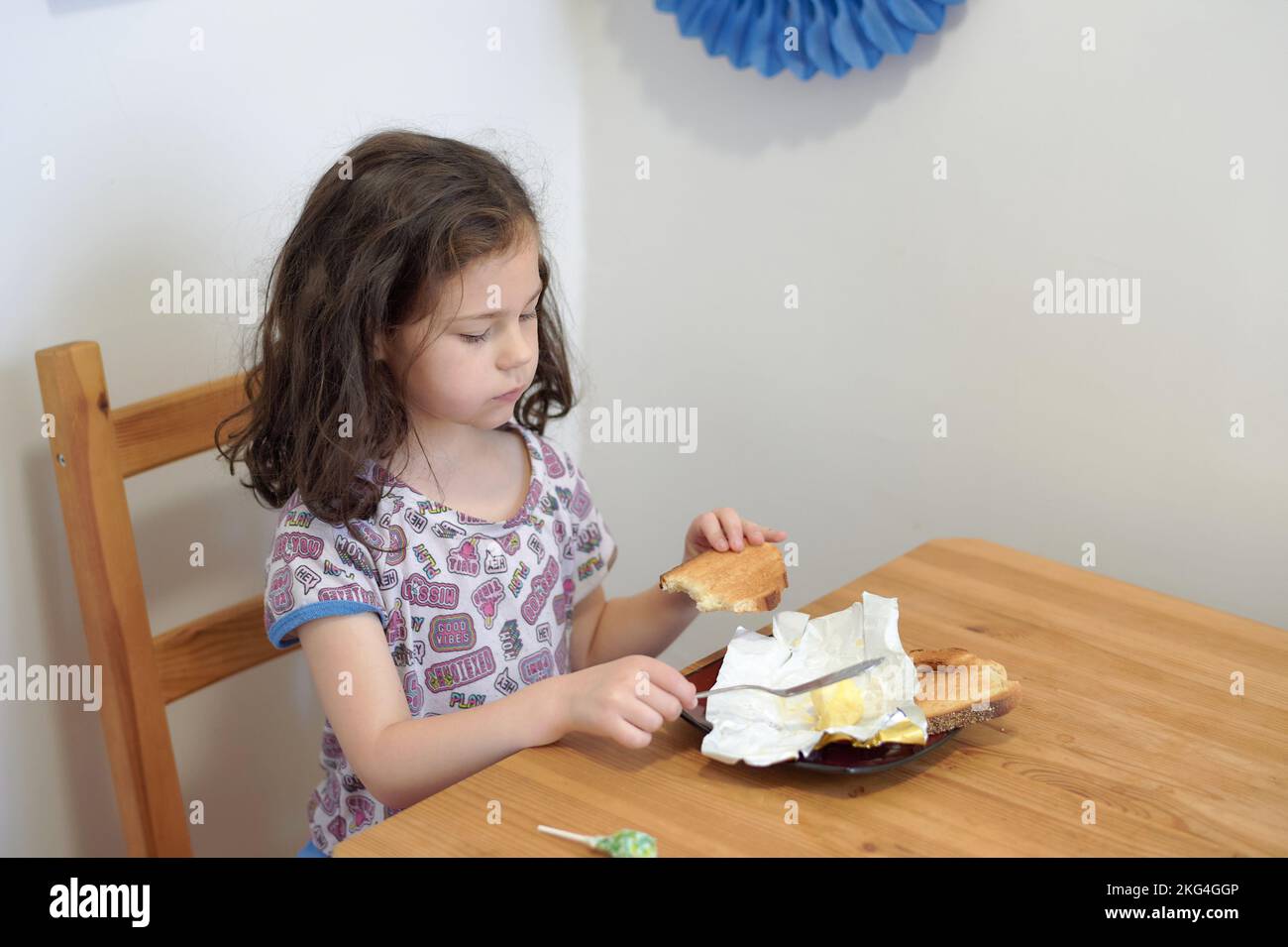 Young girl eating toast with butter at the kitchen table for breakfast ...