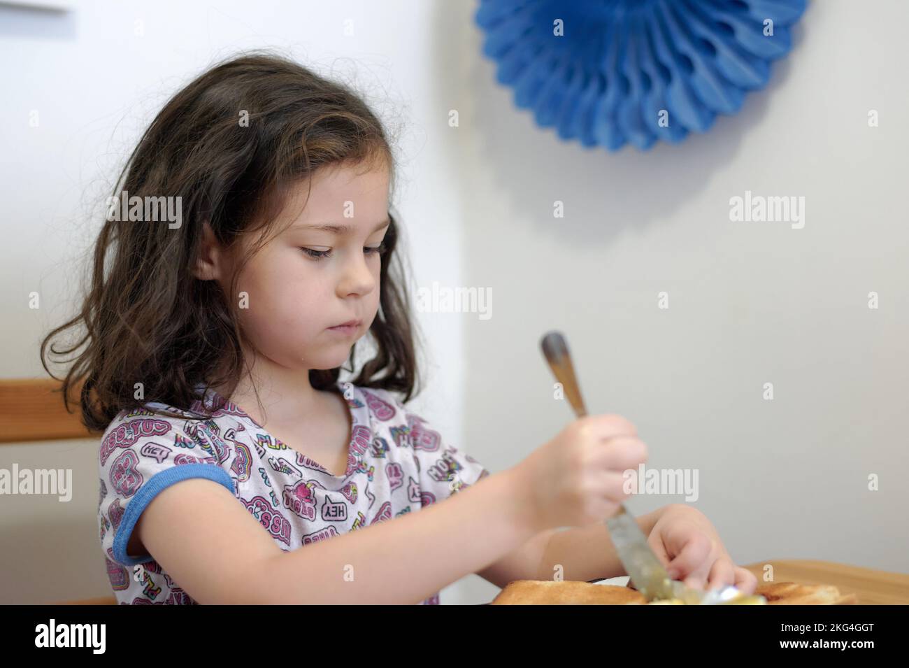 Young girl eating toast with butter at the kitchen table for breakfast ...