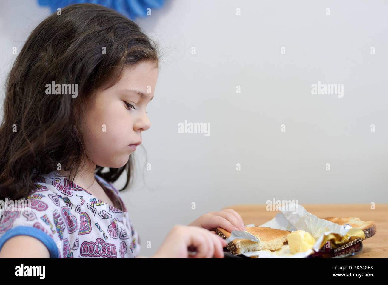 Young girl eating toast with butter at the kitchen table for breakfast ...
