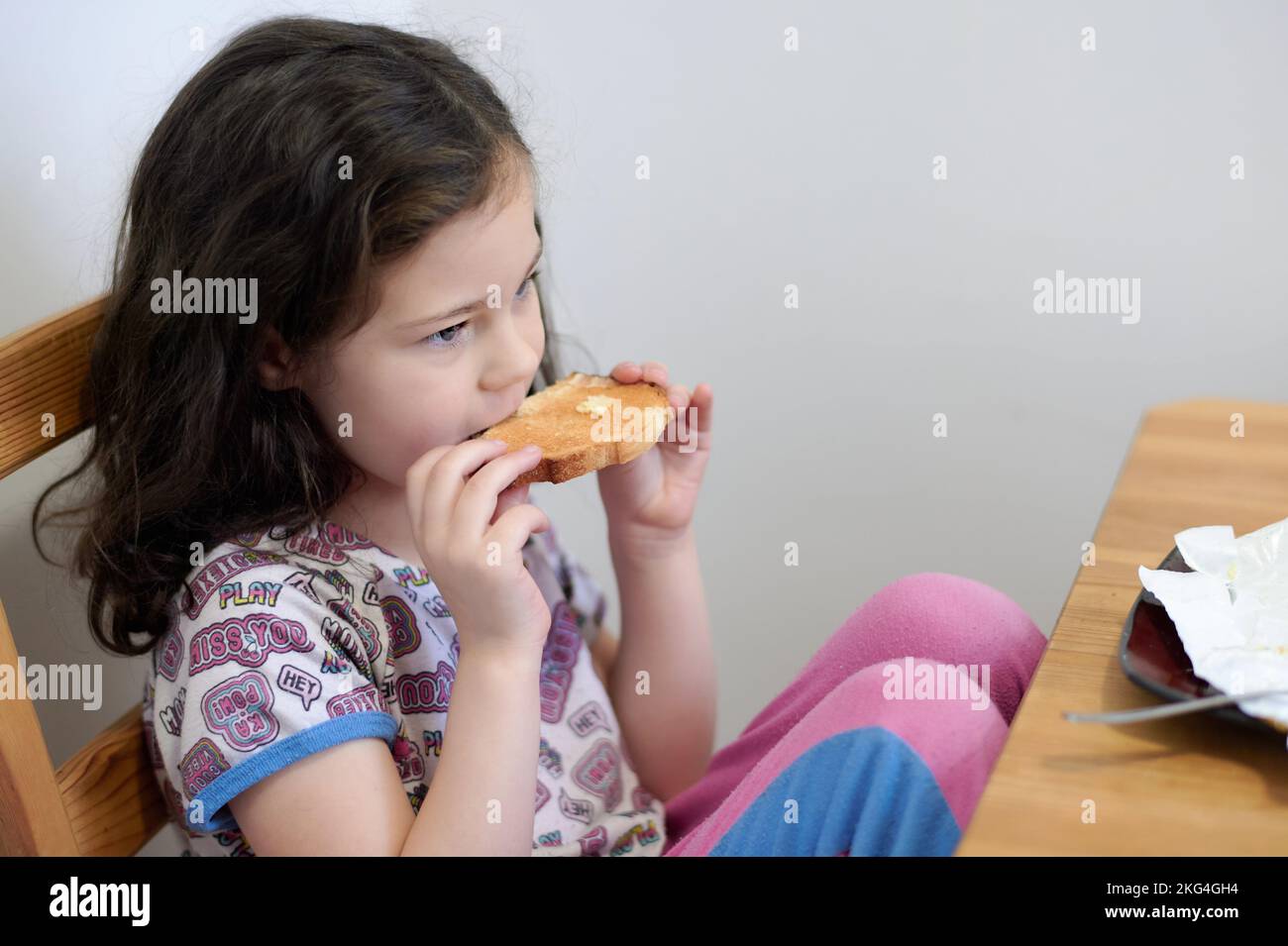 Young girl eating toast with butter at the kitchen table for breakfast ...