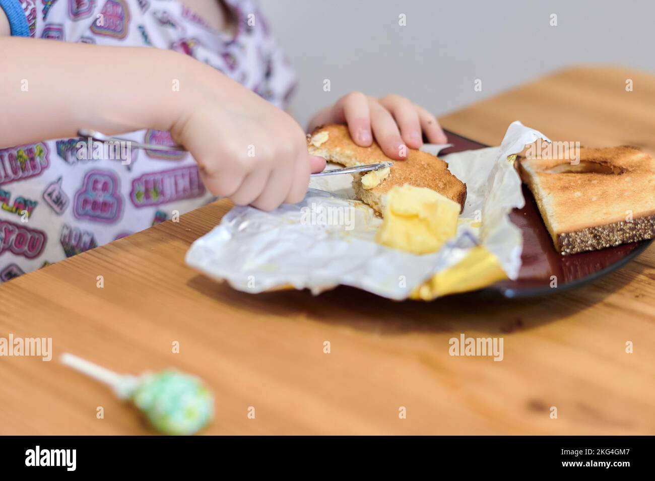 Young girl eating toast with butter at the kitchen table for breakfast ...