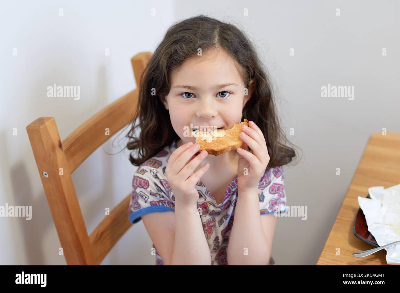 Young girl eating toast with butter at the kitchen table for breakfast ...