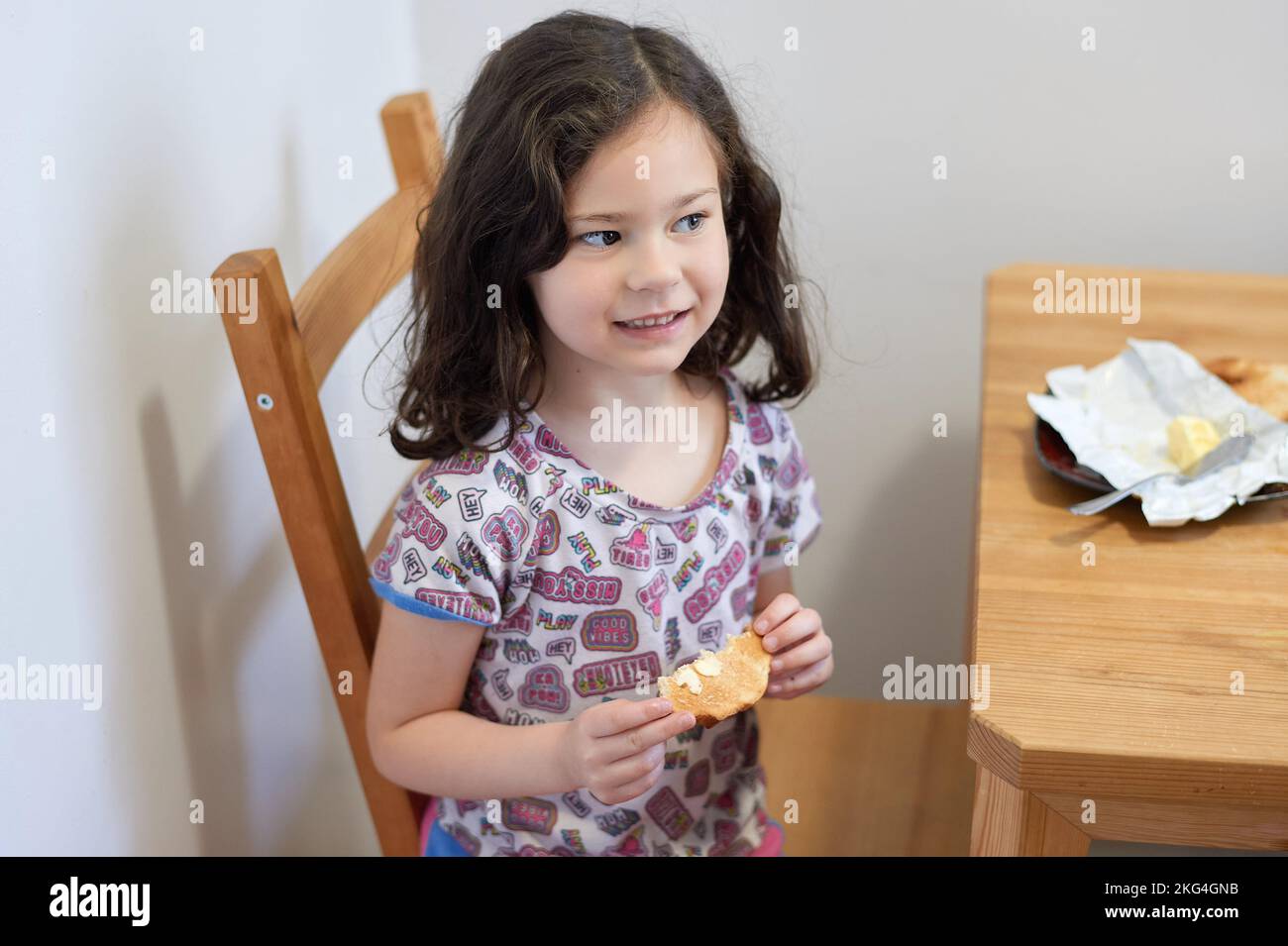 Young girl eating toast with butter at the kitchen table for breakfast ...