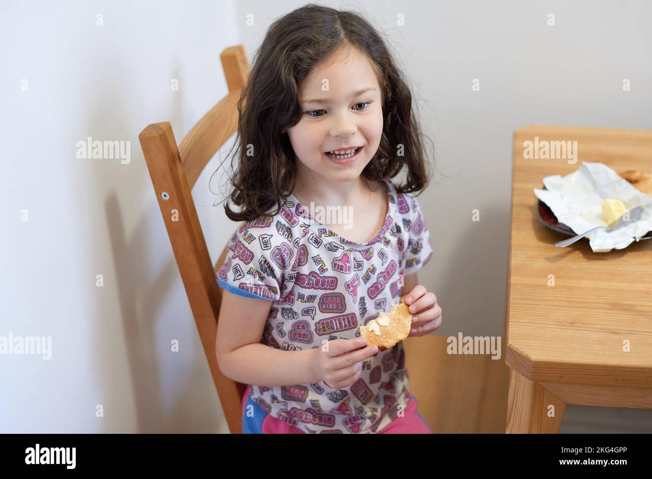 Young girl eating toast with butter at the kitchen table for breakfast ...
