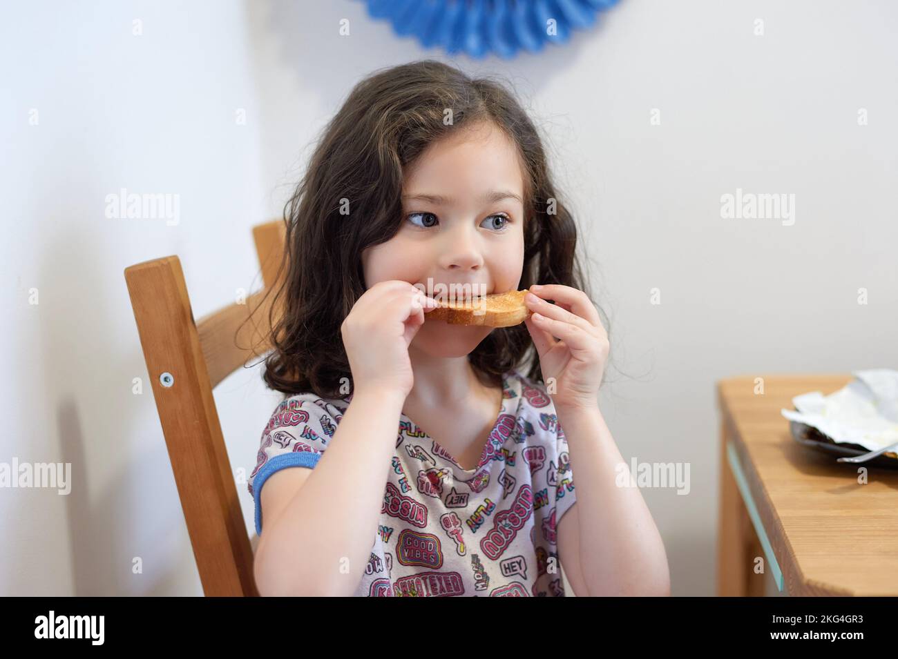 Young girl eating toast with butter at the kitchen table for breakfast ...