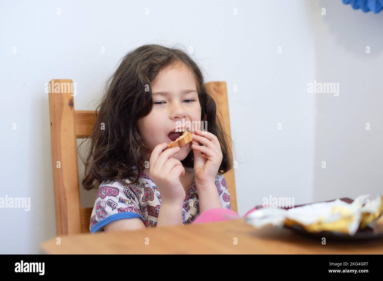 Young girl eating toast with butter at the kitchen table for breakfast ...
