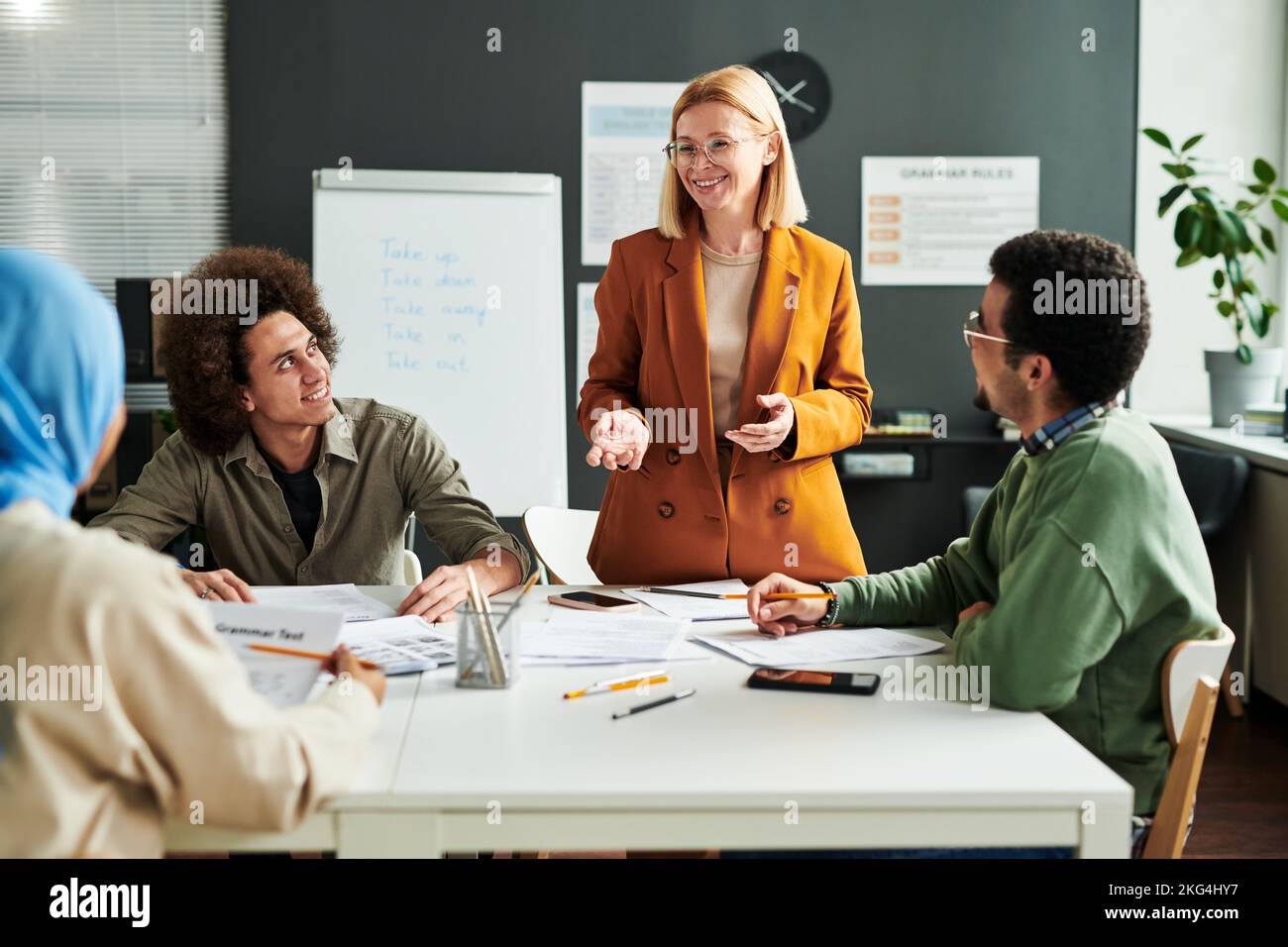 Happy mature teacher standing in front of intercultural students at ...