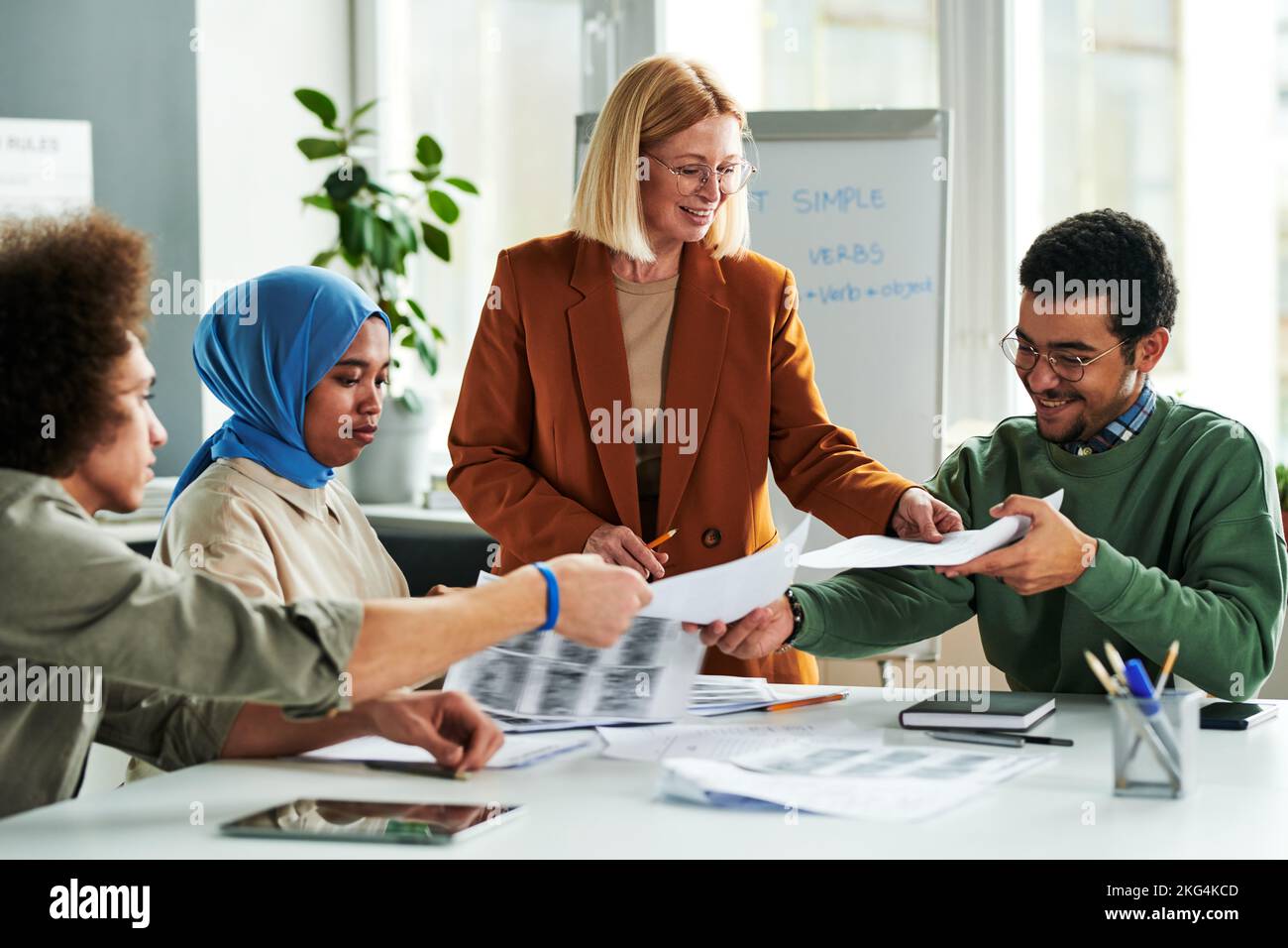 Happy mature teacher passing papers with grammar tests to group of ...