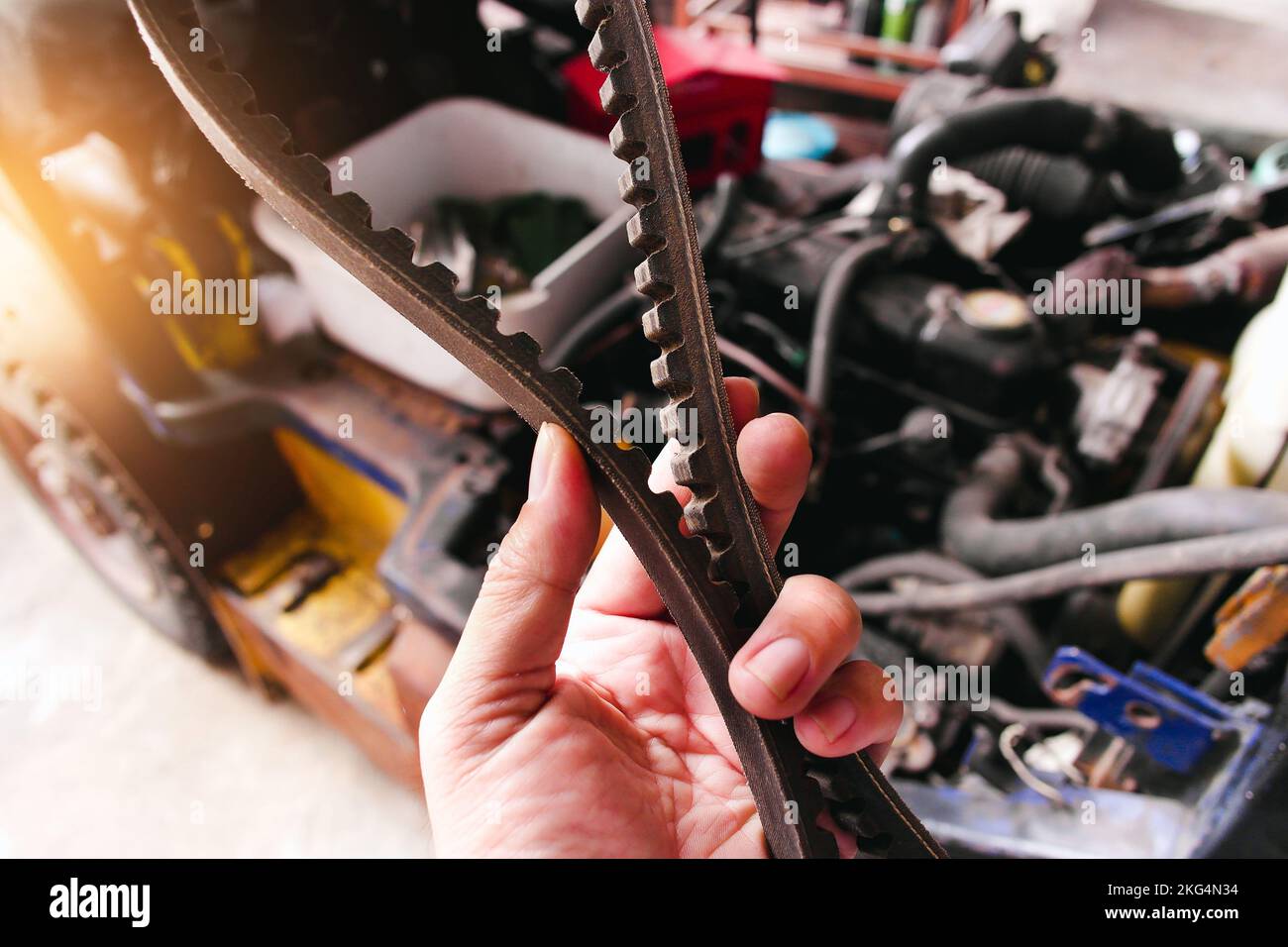 A mechanic hand holding a timing belt with a car engine is blurred in ...