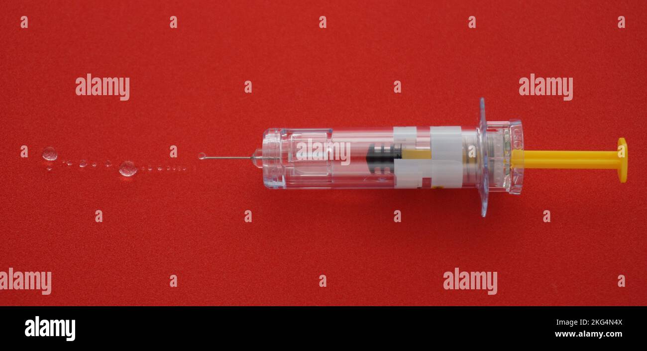 A droplet of water near the hypodermic needle agianst a red background ...