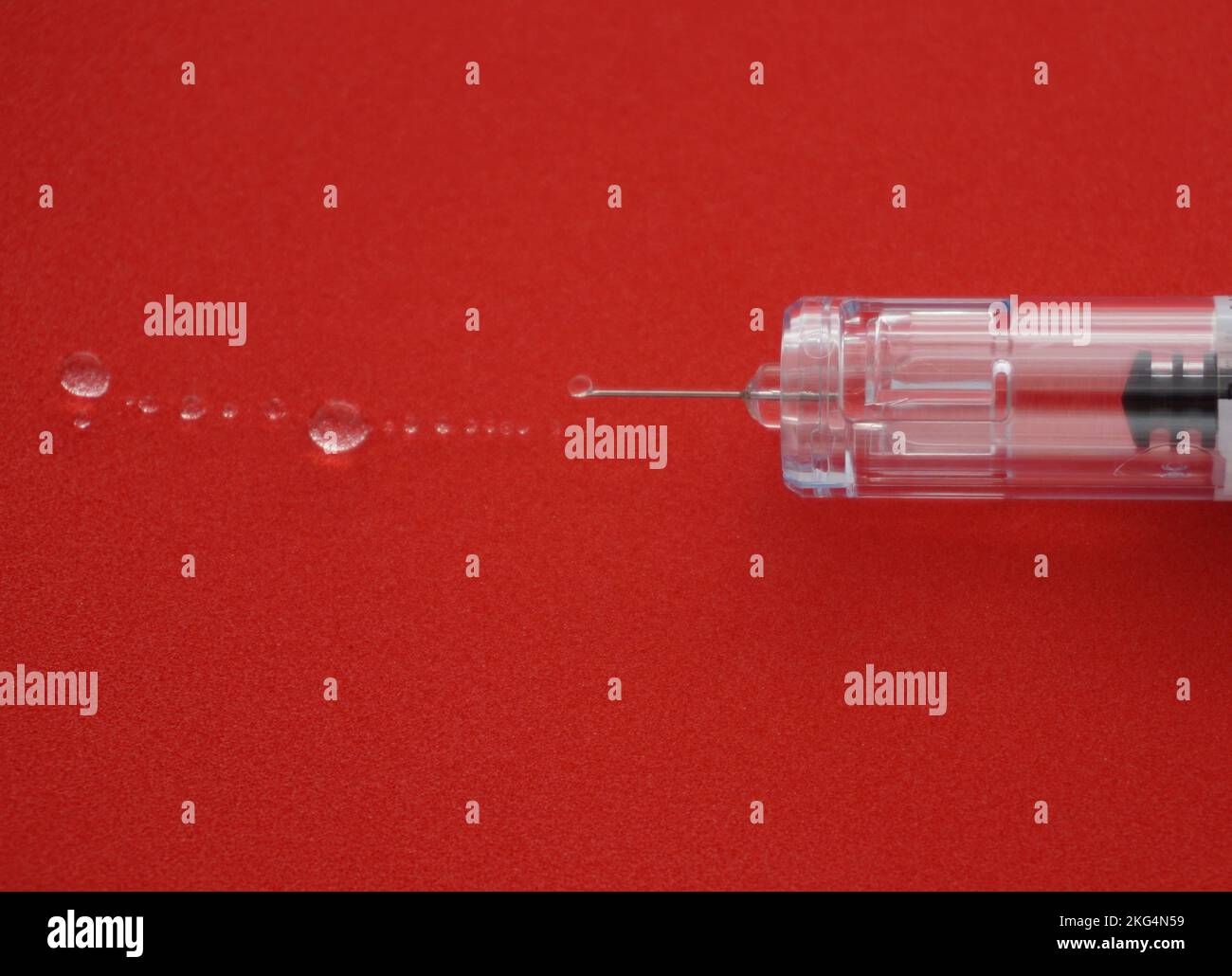 A droplet of water near the hypodermic needle agianst a red background ...