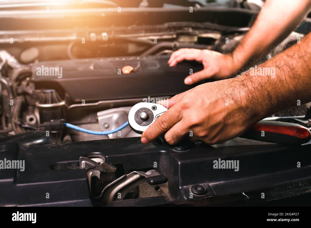 The mechanic is holding a metal socket wrench and putting his hand on ...