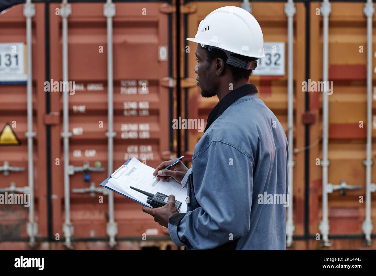 Side view portrait of young male worker wearing writing on clipboard in ...