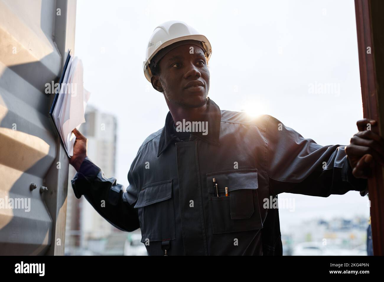 Backlit portrait of male worker wearing hardhat opening container door ...