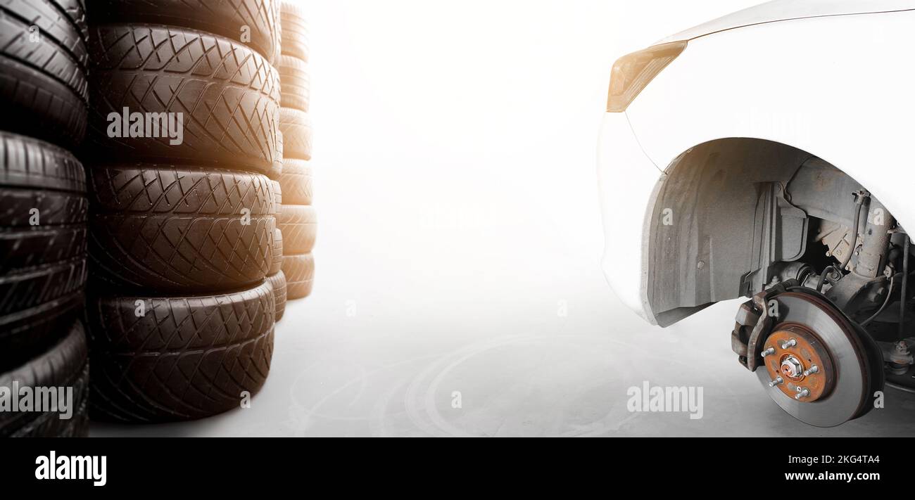 A pile of automobile tyre and white car without wheel with sunlight and ...