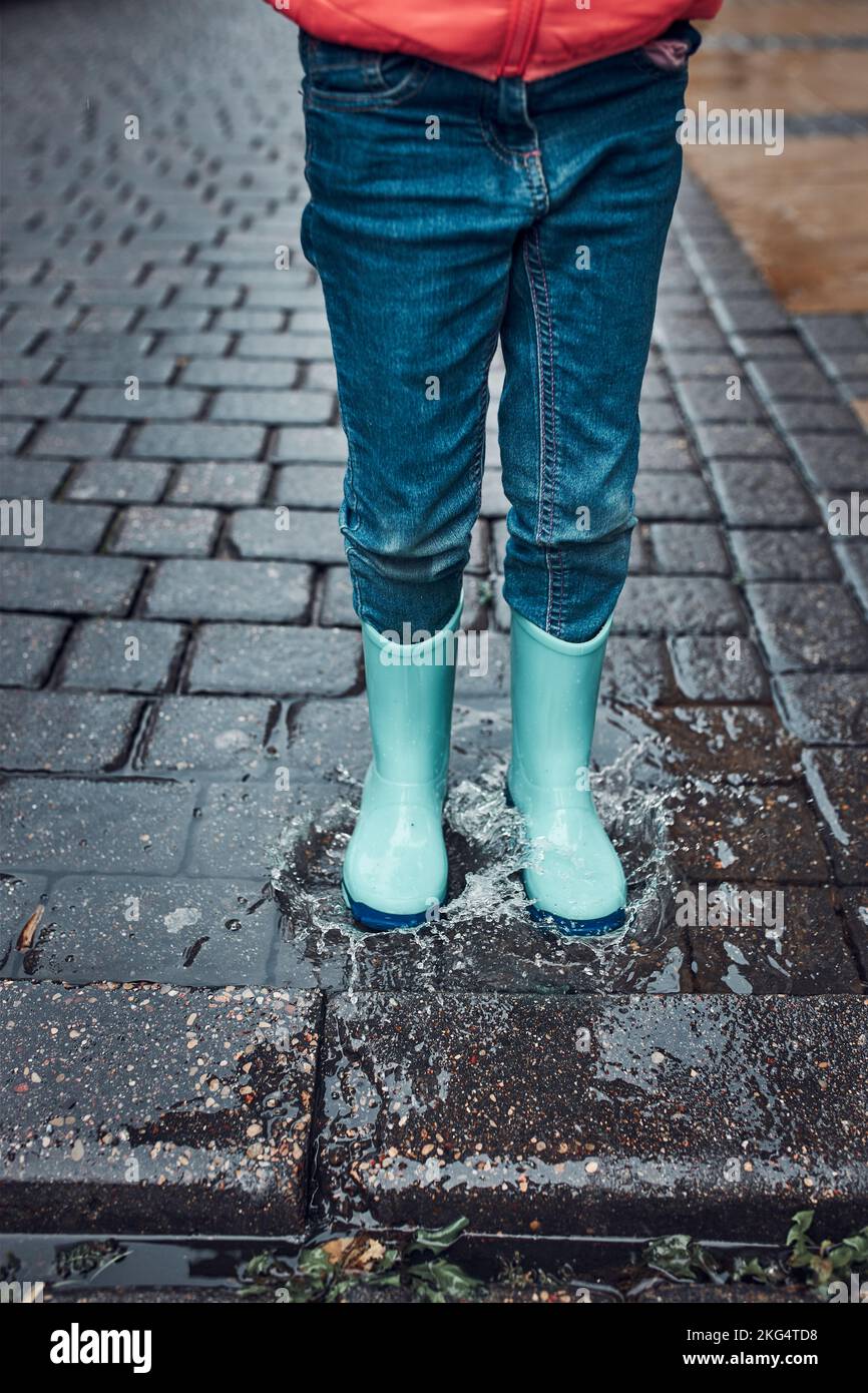 Close up of legs of little girl jumping in puddle wearing rubber boots ...