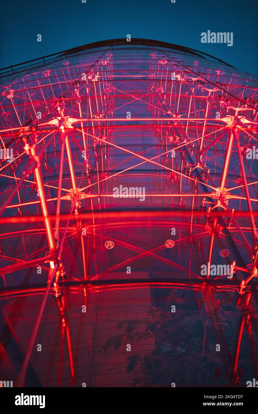 Looking up at modern glass building lighted with red at night. View ...